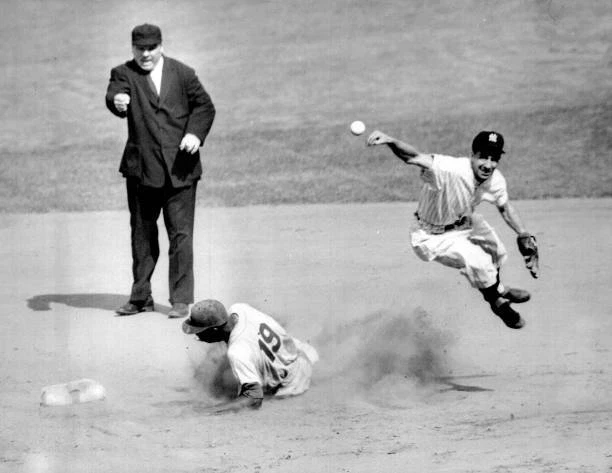 PHIL RIZZUTO OF the New York Yankees leaps high to avoid spikes of ...